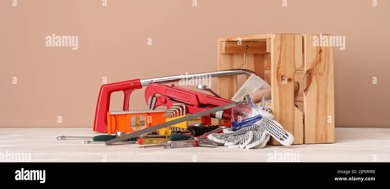 Overturned box with different construction tools on table against beige ...