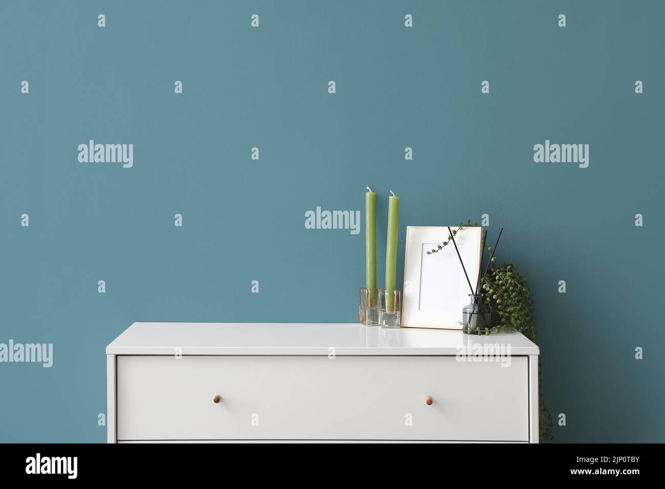 Candles, frame, reed diffuser and houseplant on chest of drawers ...