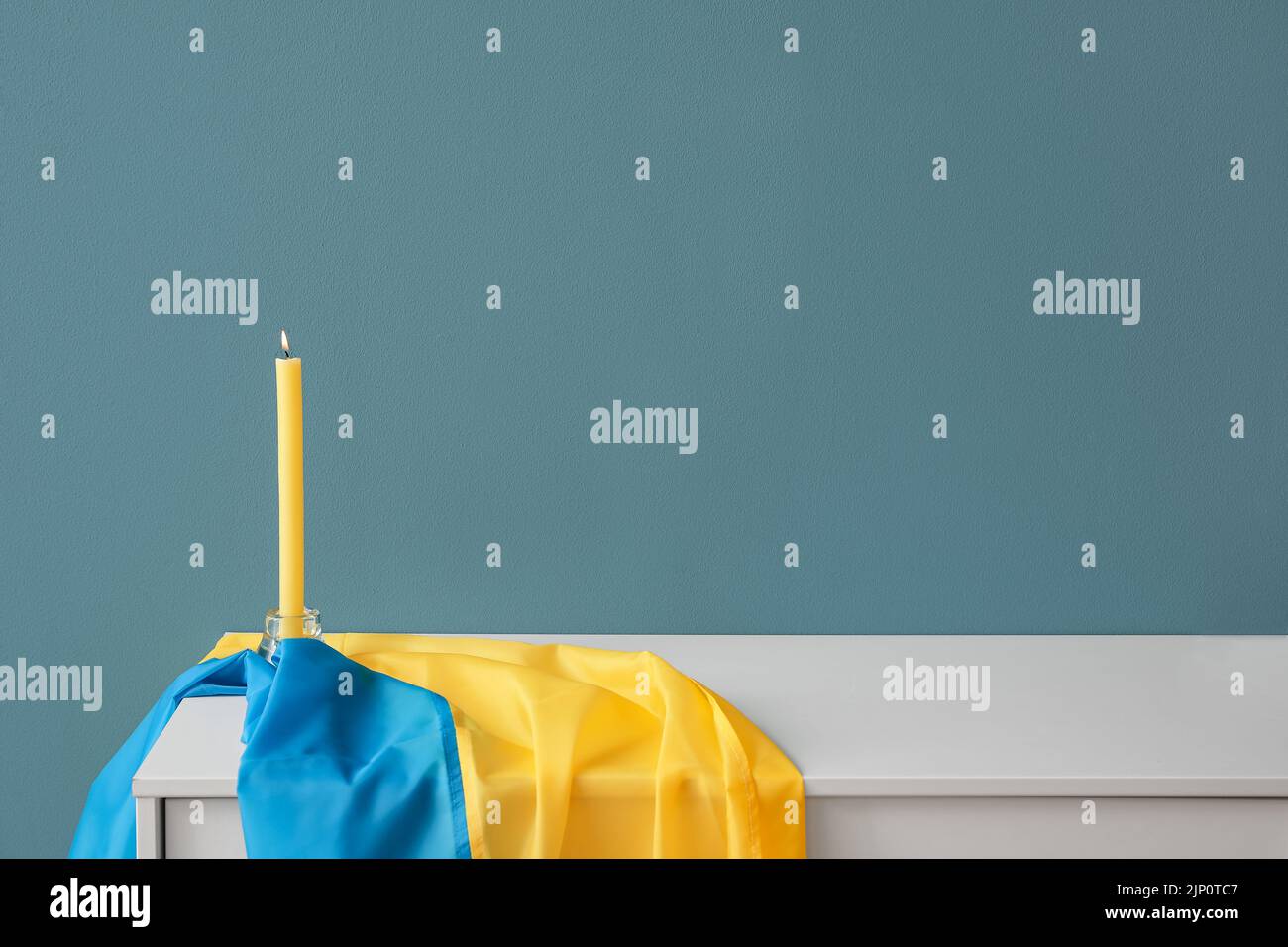 Burning candle and flag of Ukraine on table against blue background ...