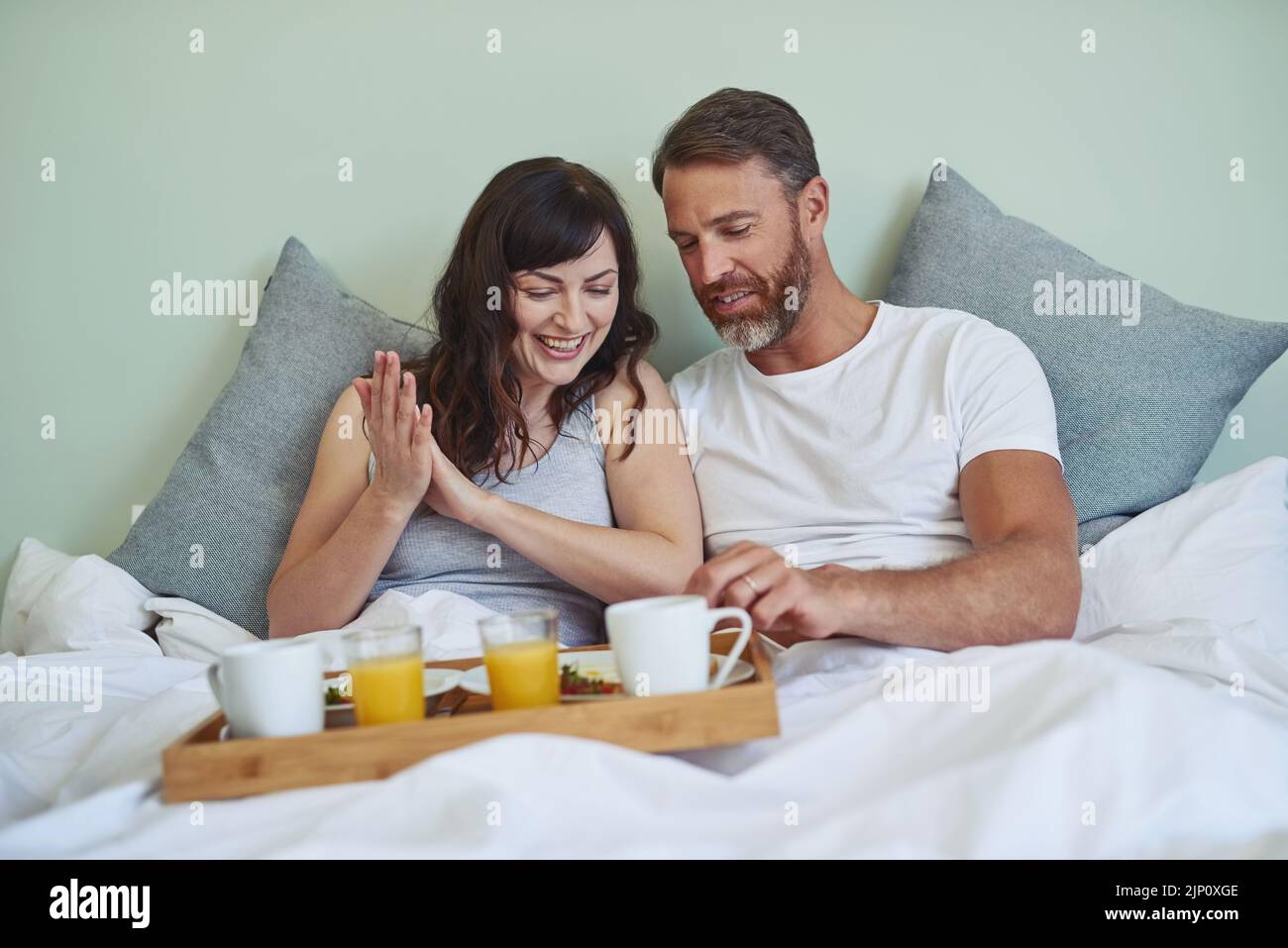 Lets dig in. a cheerful young couple sitting in bed while enjoying ...