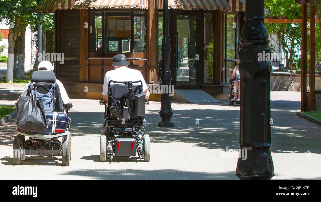 Two disabled person on an electric wheelchair on a city street . The ...