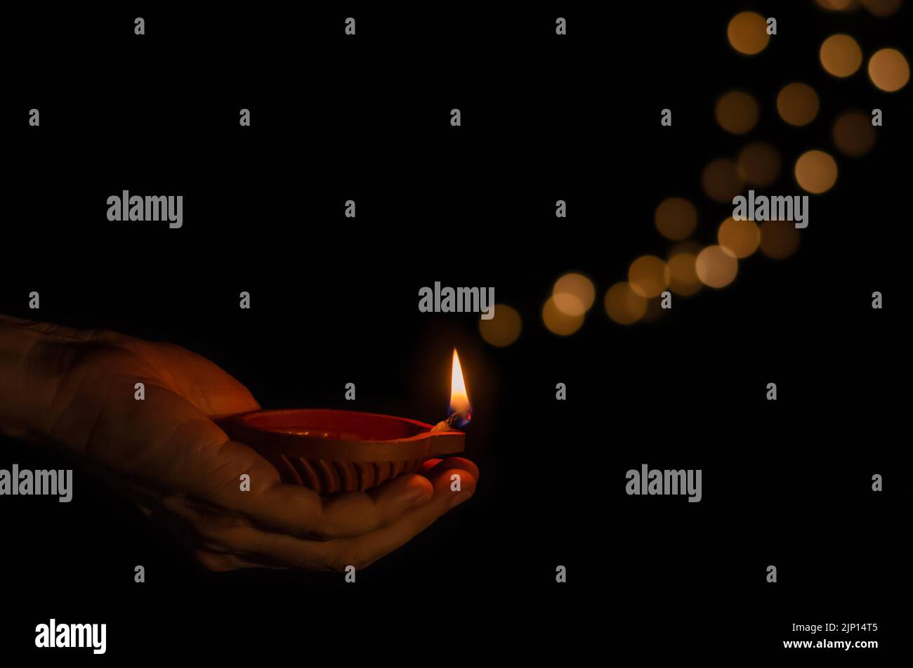 Hand holding the clay diya lamp lit on dark background with bokeh ...