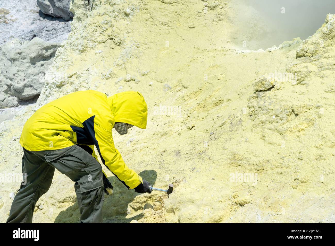 male volcanologist on the slope of a volcano next to a smoking fumarole ...