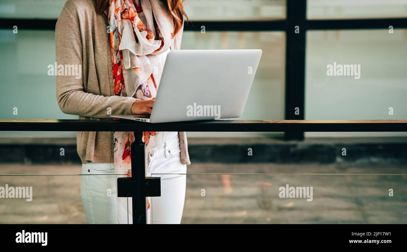 Confident young woman working on laptop while sitting near window in ...