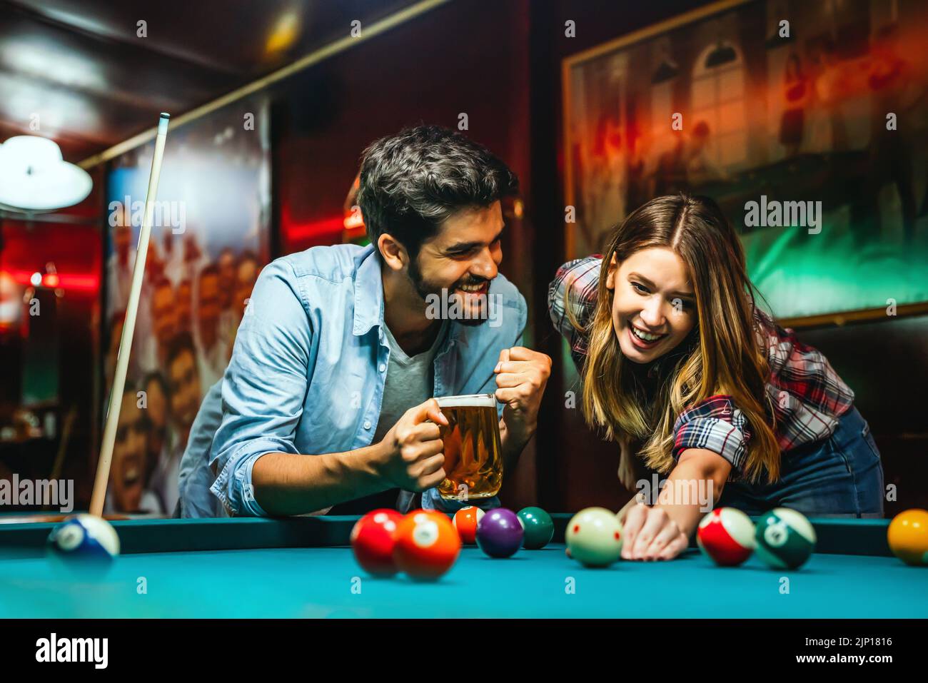 Happy young couple enjoying while playing billiard in bar. People ...