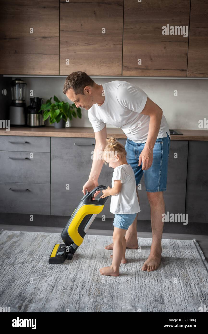Father and daughter having fun with vacuum cleaner while cleaning at ...