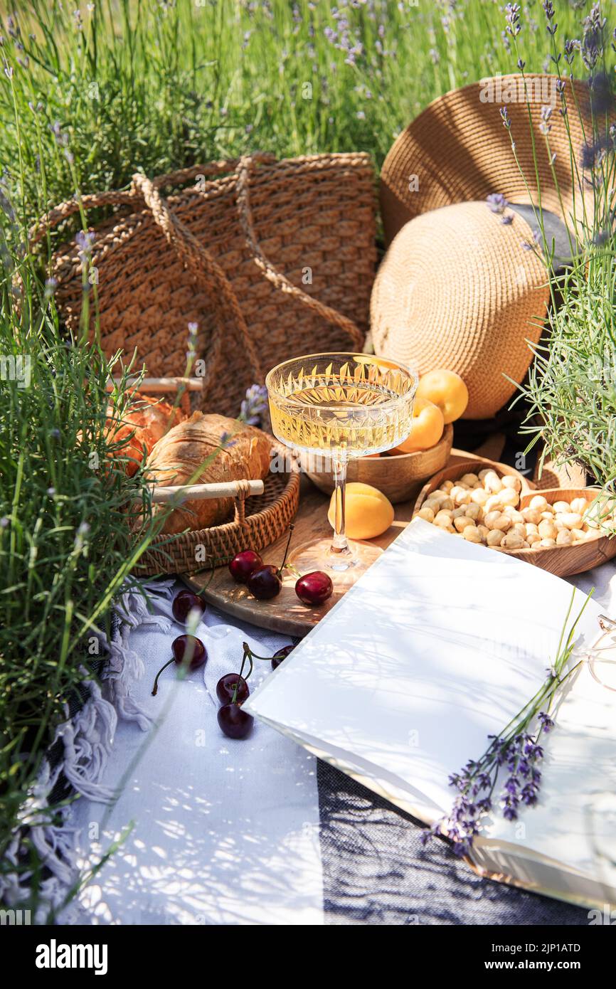Summer picnic on a lavender field with champagne glasses, croissants, apricots and cherry ...