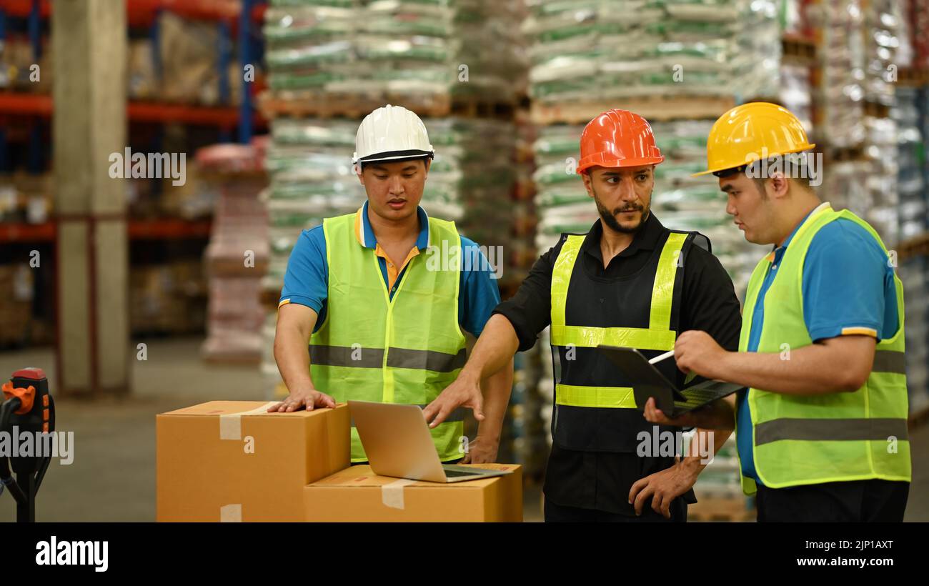 Industrial worker and manager wearing hard hat checking stock and order details in warehouse ...