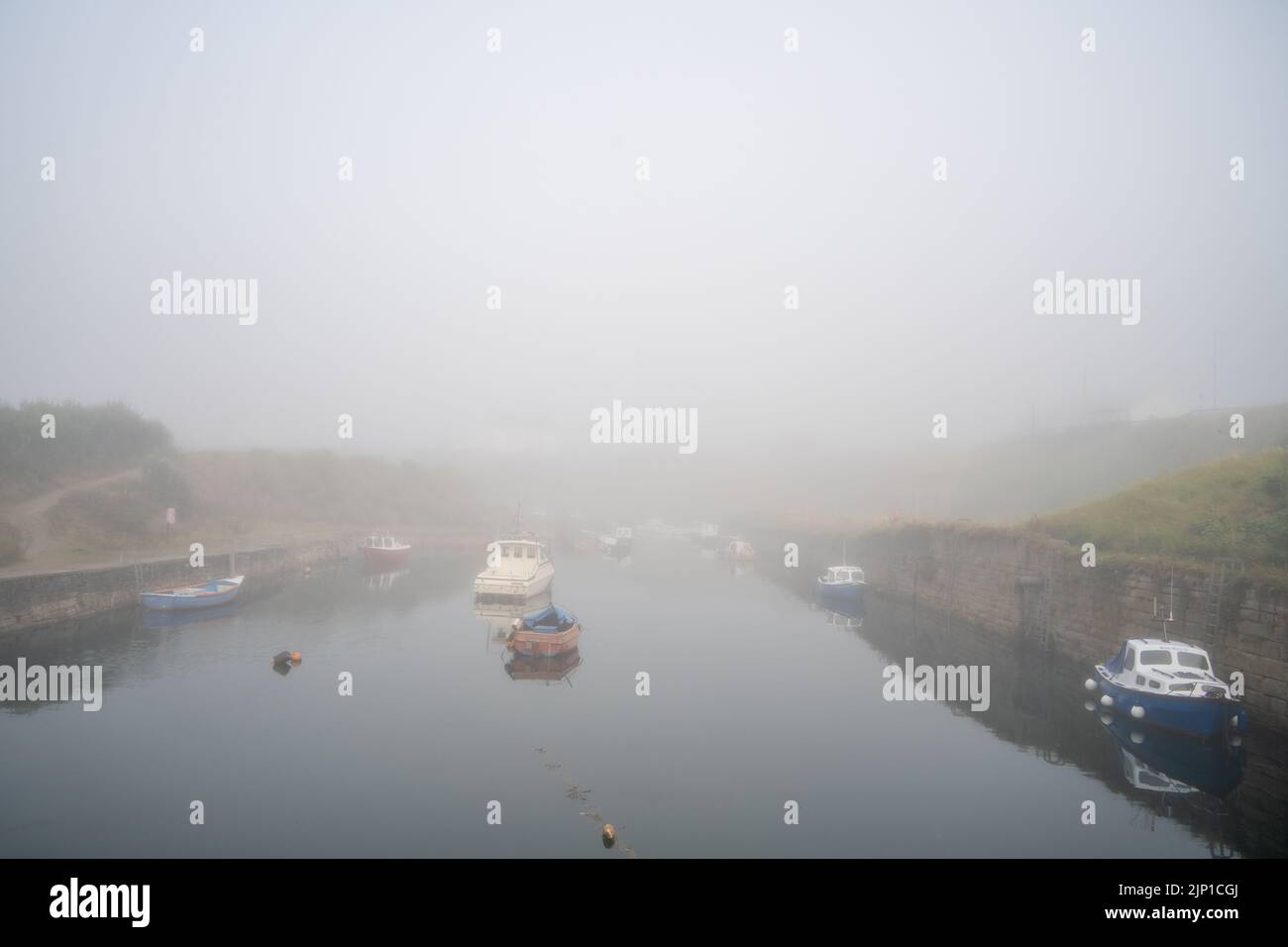 Boats in heavy sea fret at the harbour, at high tide in Seaton Sluice, Northumberland, UK, on ...