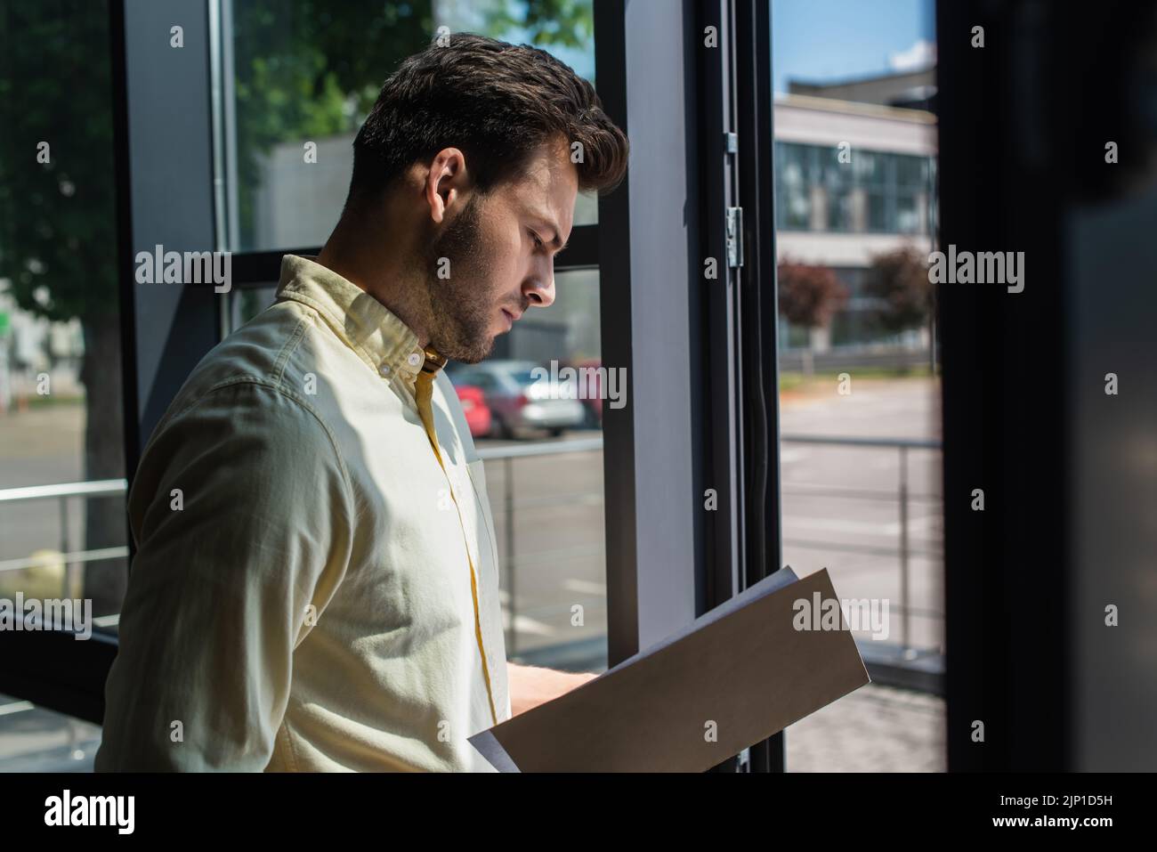 Side view of businessman looking at paper folder near window in office ...