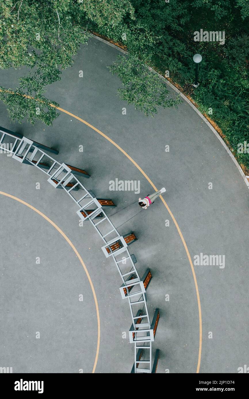 Lonely girl swings on hanging swing in park. Aerial drone view of ...