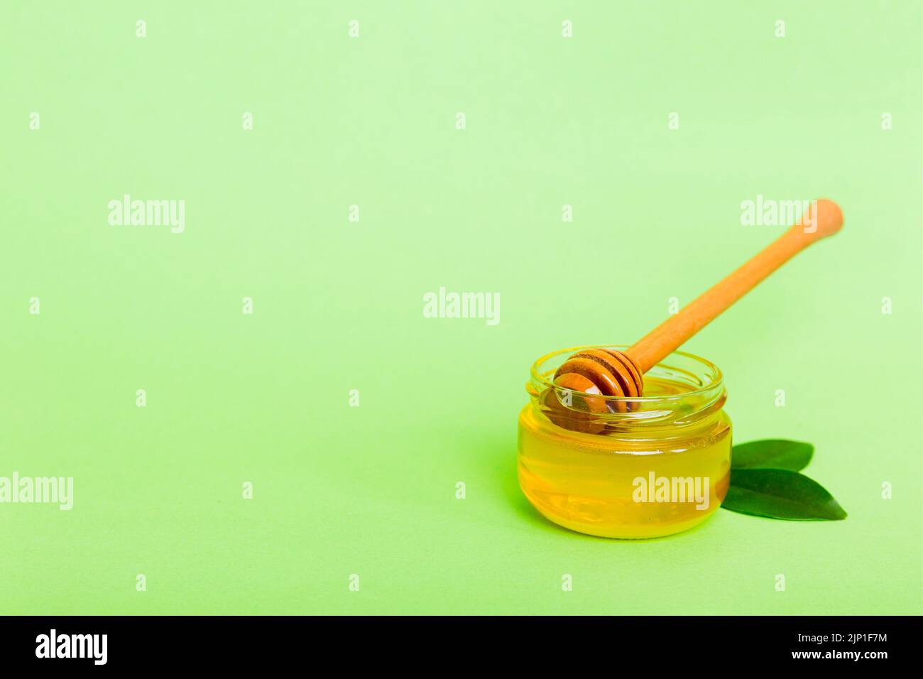 Honey in jar with leaves and honey dipper on colored background top ...