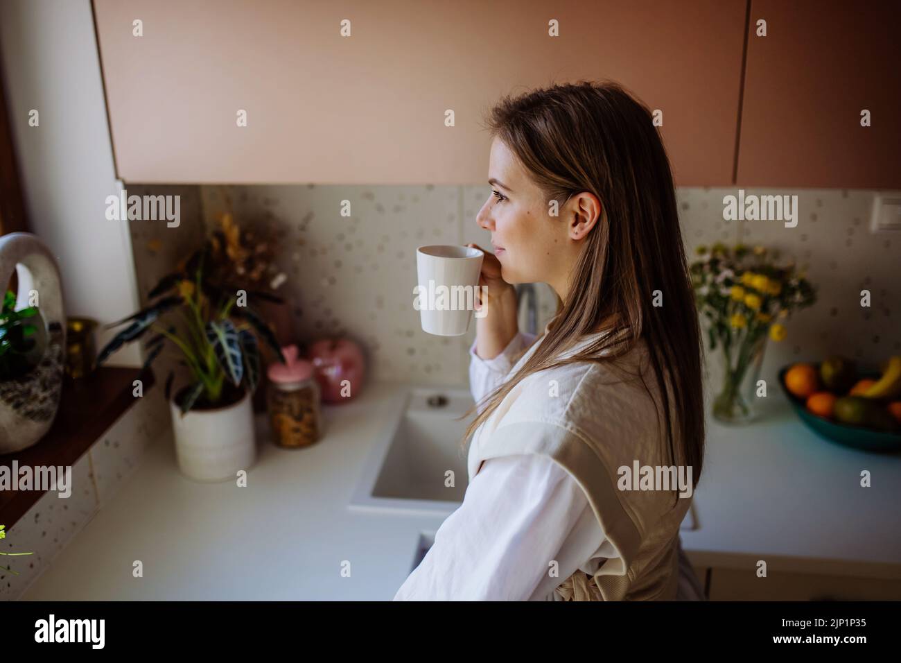 Smiling young woman with dreamy face drinking morning coffee at her ...