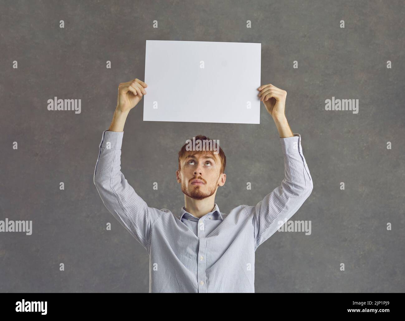 Serious young Caucasian man looks at a blank sheet of paper he is ...