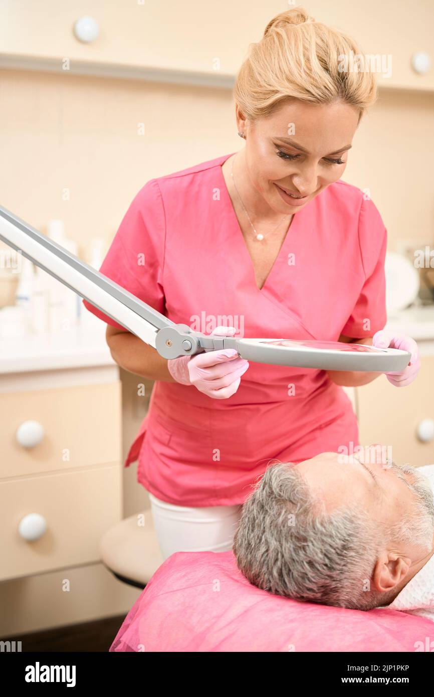 Woman cosmetologist examines skin problems in man through magnifying ...