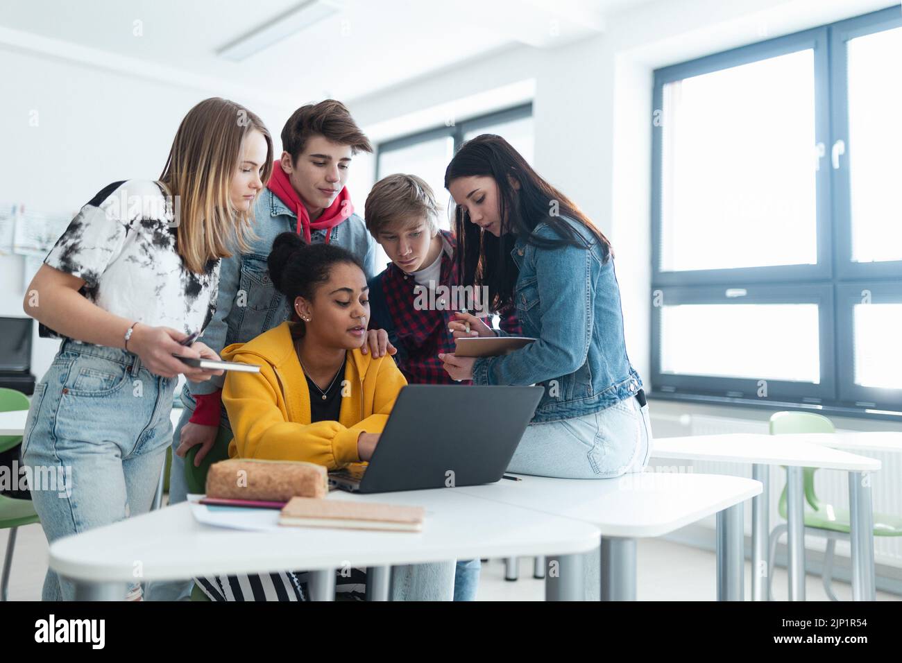 High school students sitting together at desk and using laptop and ...