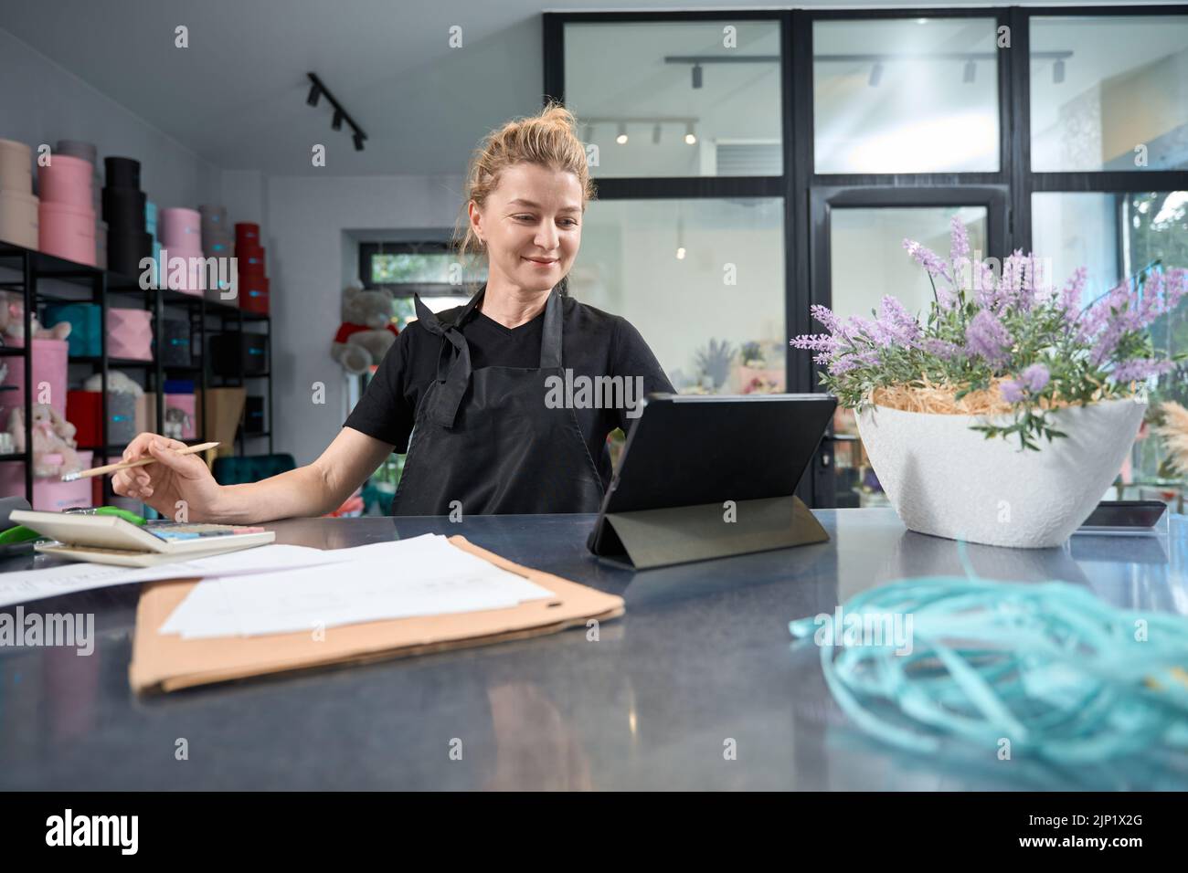 Smiling female florist looking at tablet and counting sales, orders ...