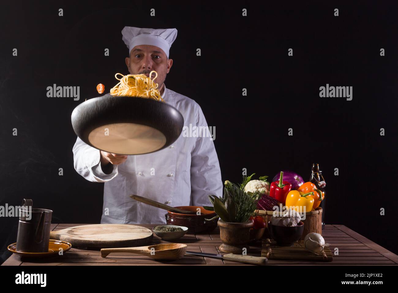 Male chef in white uniform holding a frying pan, sautéing spaghetti ...