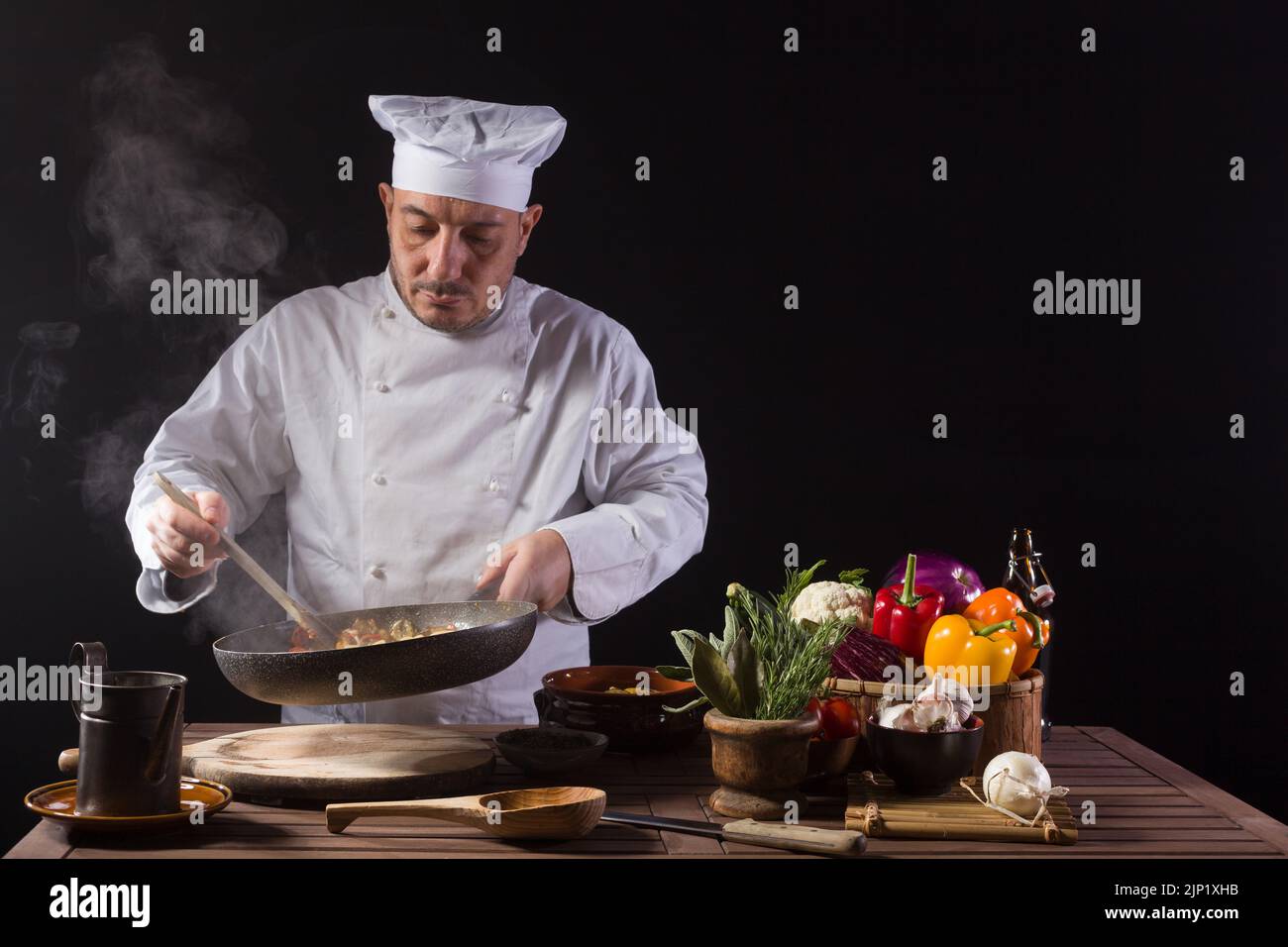 Male cook in white uniform and hat with ladle mixes the ingredients ...