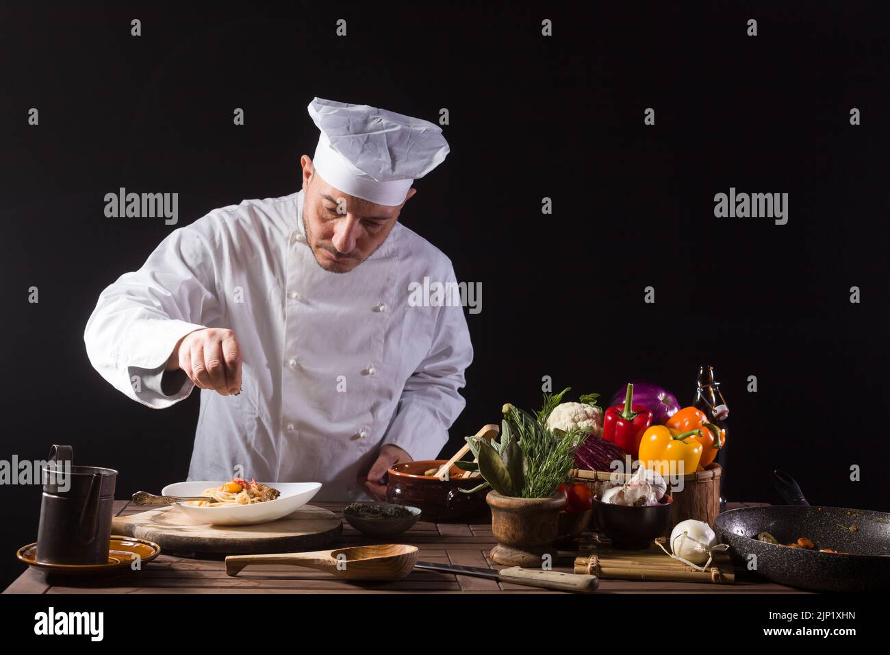 Male cook in white uniform and hat putting pot herbs on on food plate ...