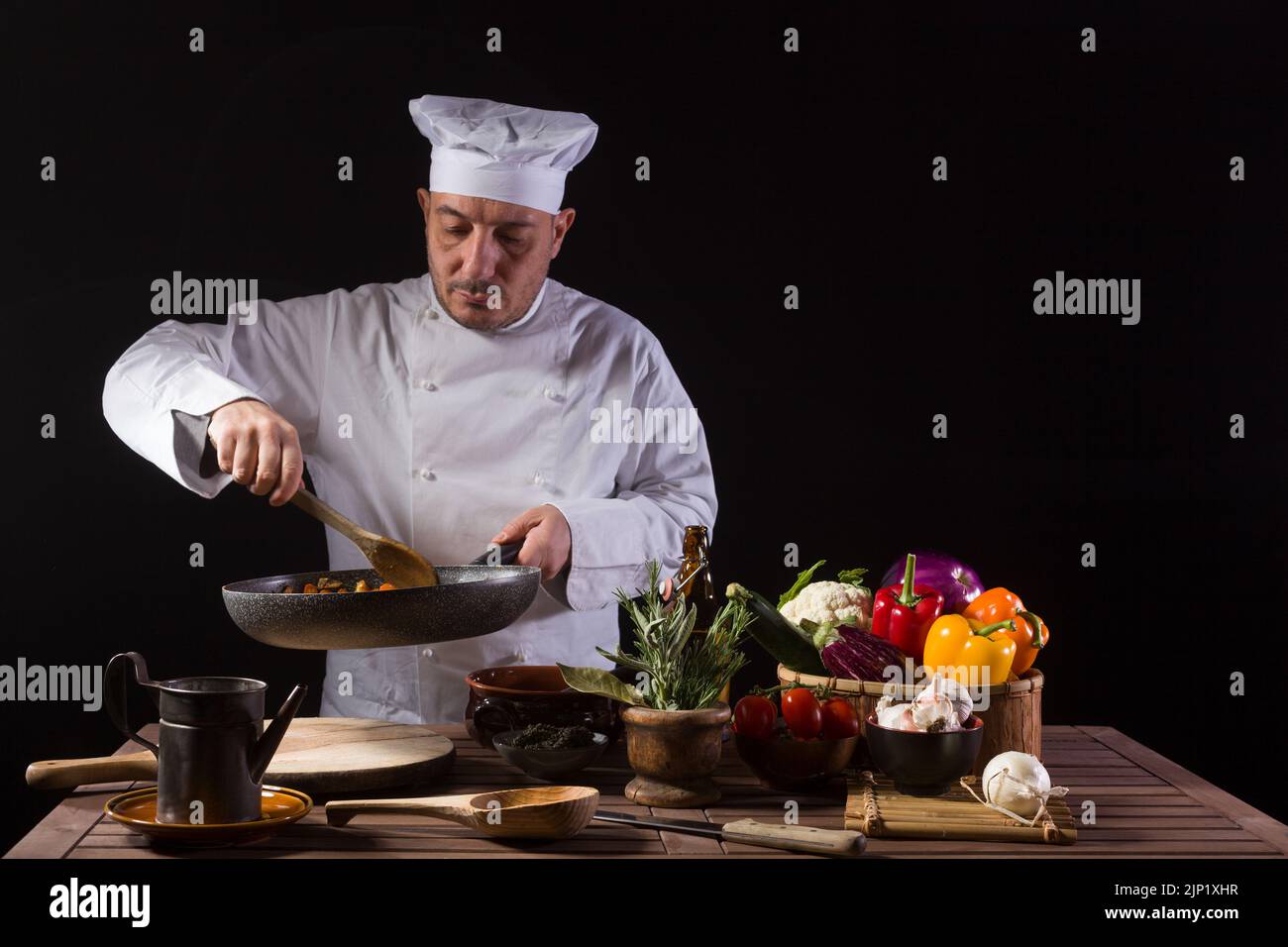 Chef in white uniform and hat with ladle mixes the ingredients onto the ...