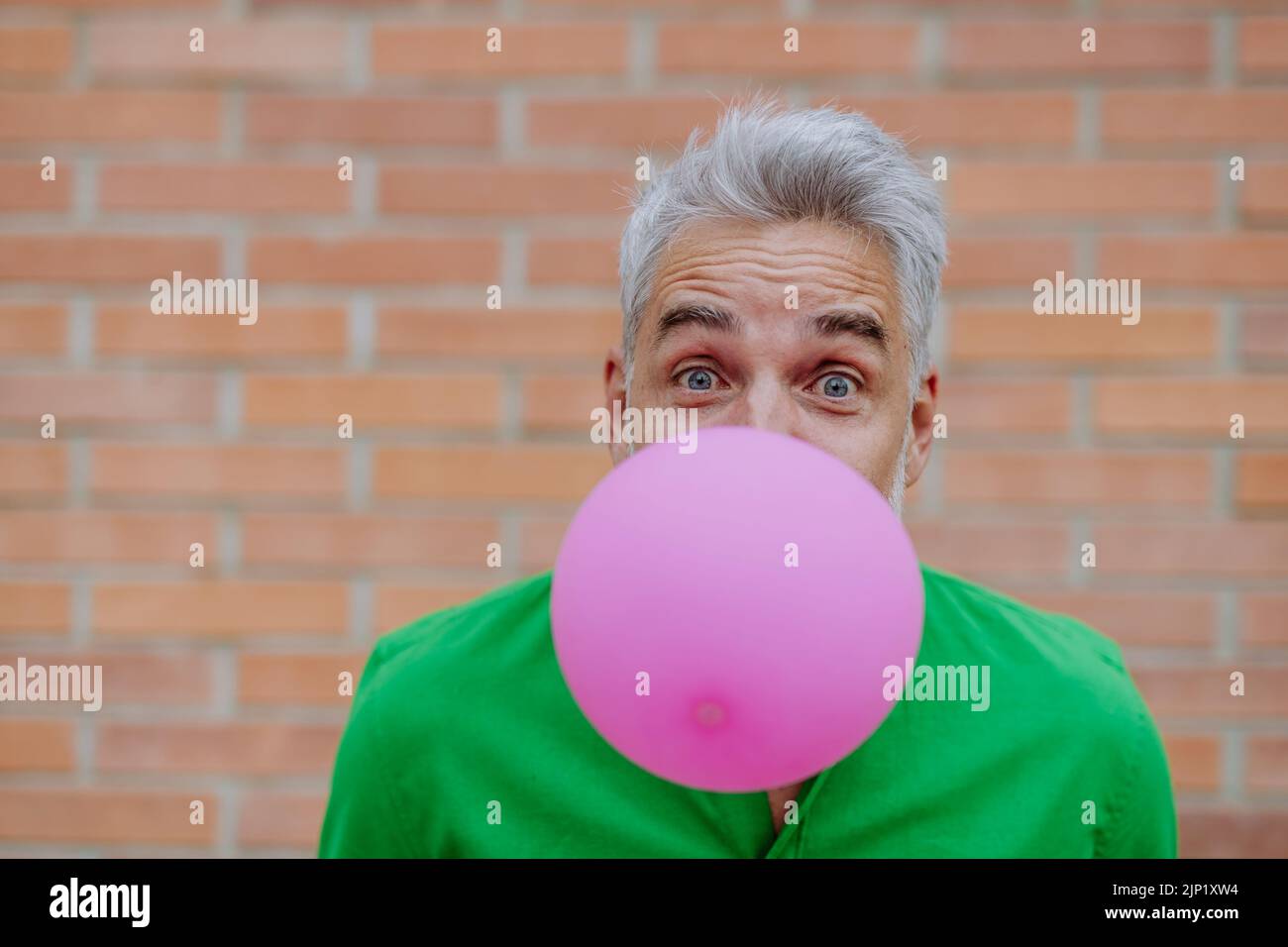 Fun portrait of happy energetic mature man inflating pink balloon in ...
