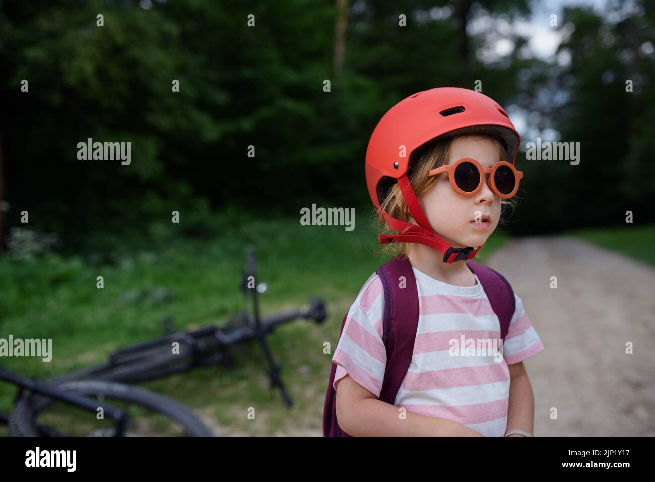 Portrait of little girl in red bicycle helmet waiting on forest path in ...