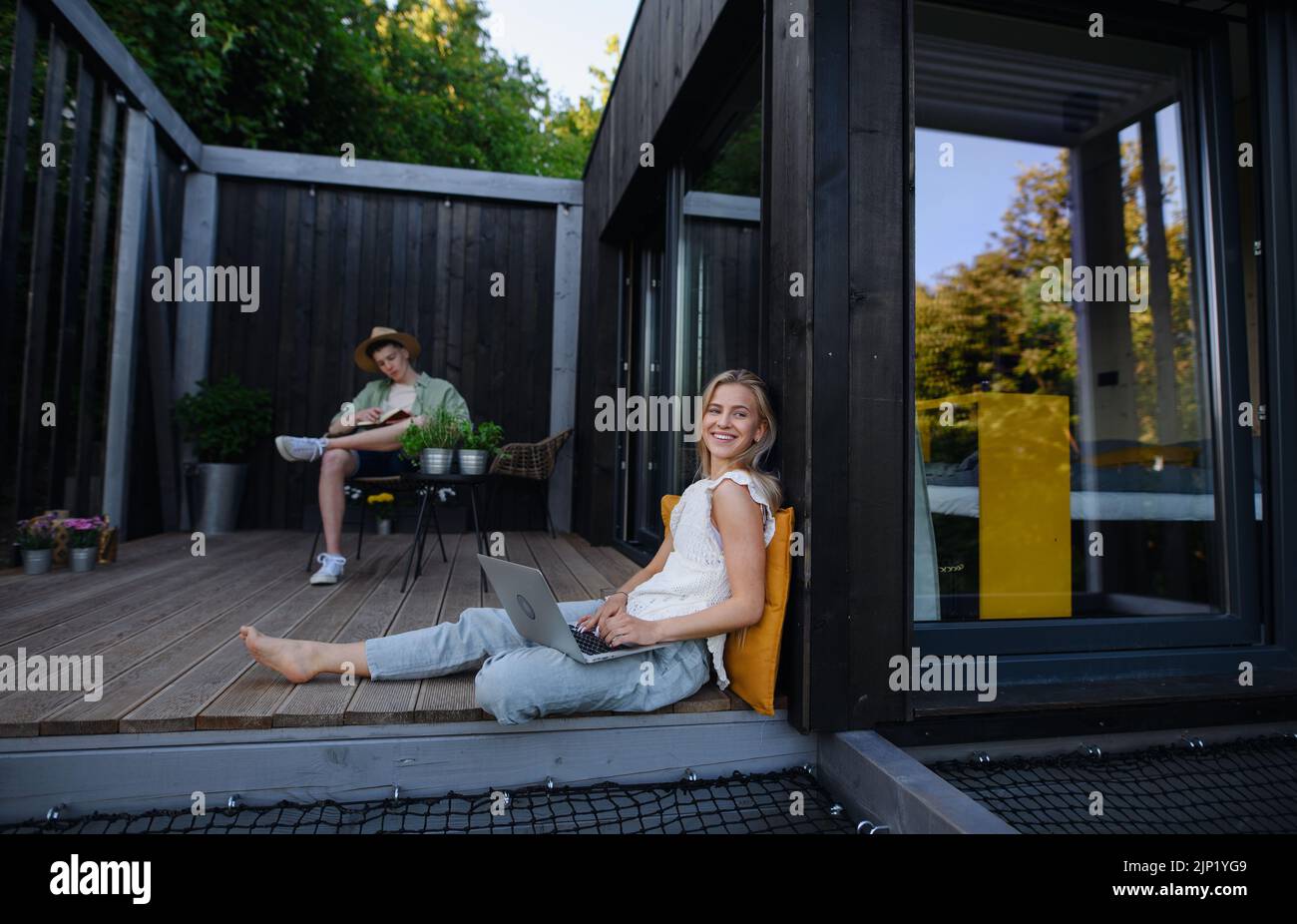 Happy young couple with laptop resting outdoors in a tiny house ...