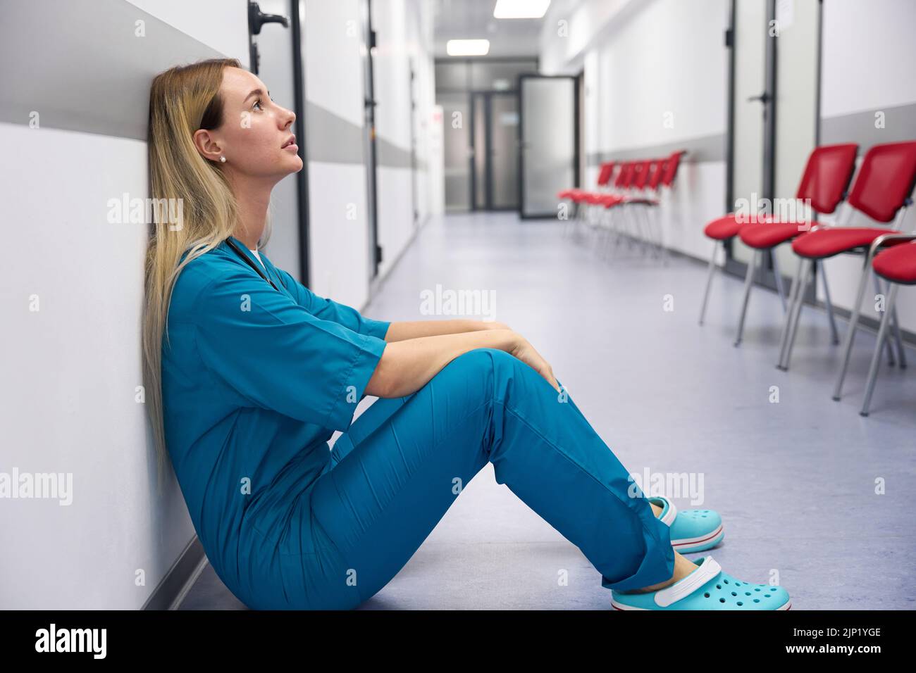 Doctor sits on the floor in the corridor leaning against the wall ...