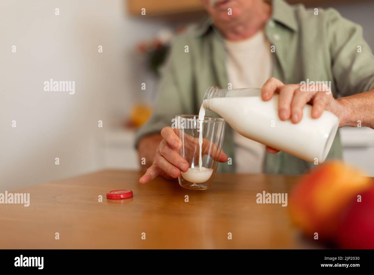 Close up of senior man sitting in kitchen and pouring milk in his glass ...