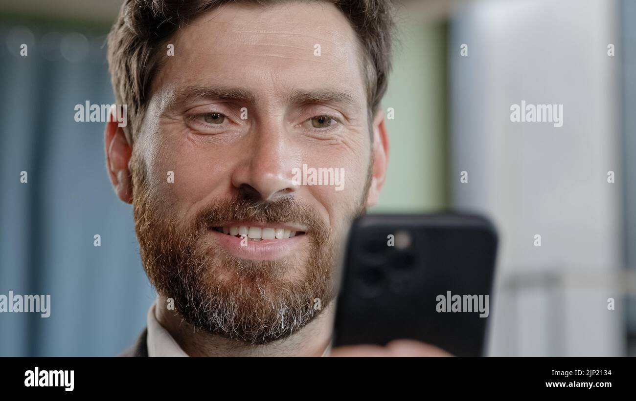 Close up head shot smiling bearded adult 40s businessman holding smartphone in office smile ...