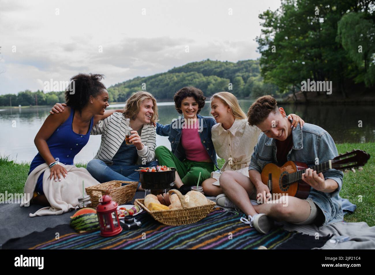 Group of friends having fun on picnic near a lake, sitting on blanket ...