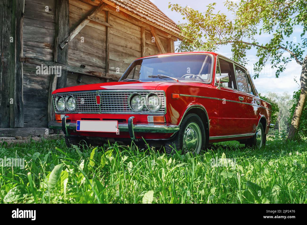 Close-up view of red vintage Lada car in countryside. Old wooden barn ...