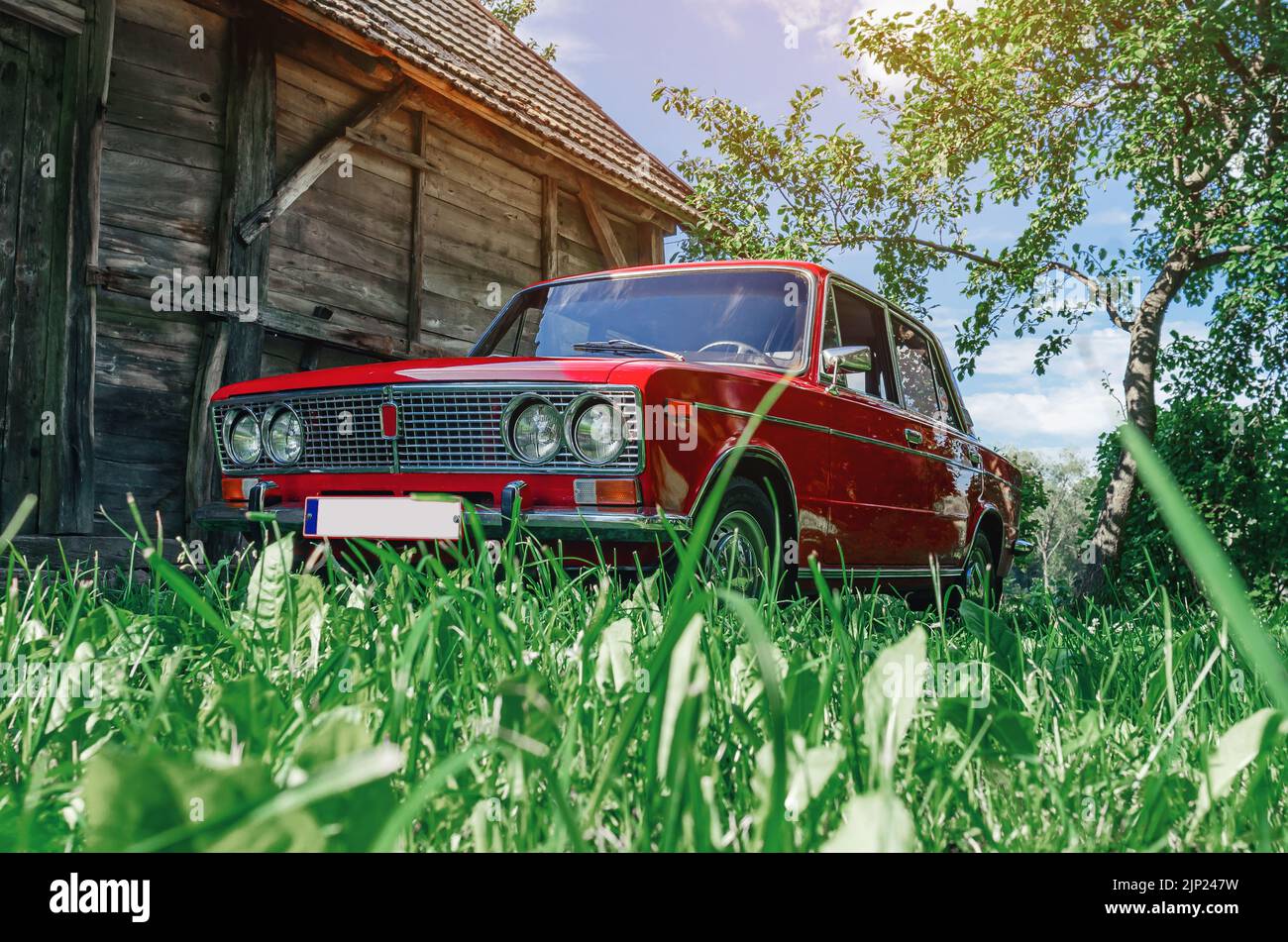 Close-up view of red vintage Lada car in countryside. Old wooden barn ...
