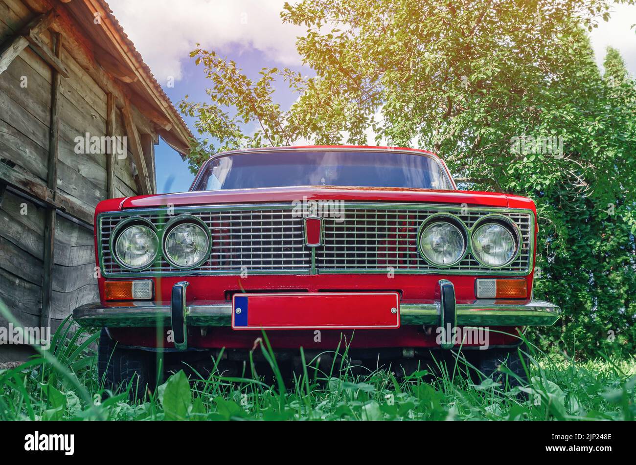 Front view of red vintage Lada car in countryside. Old wooden barn from ...