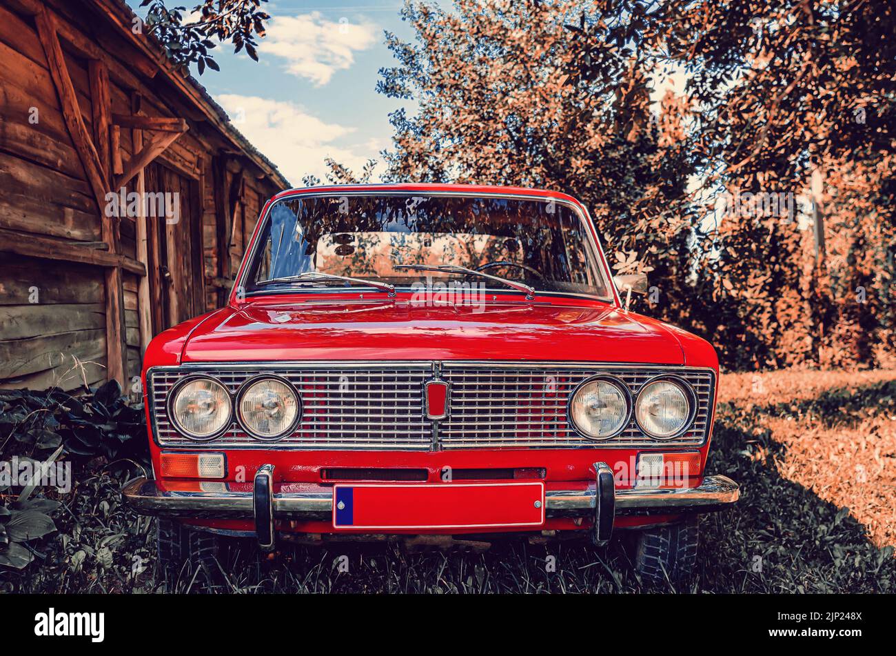 Front view of red vintage Lada car in countryside. Old wooden barn from ...