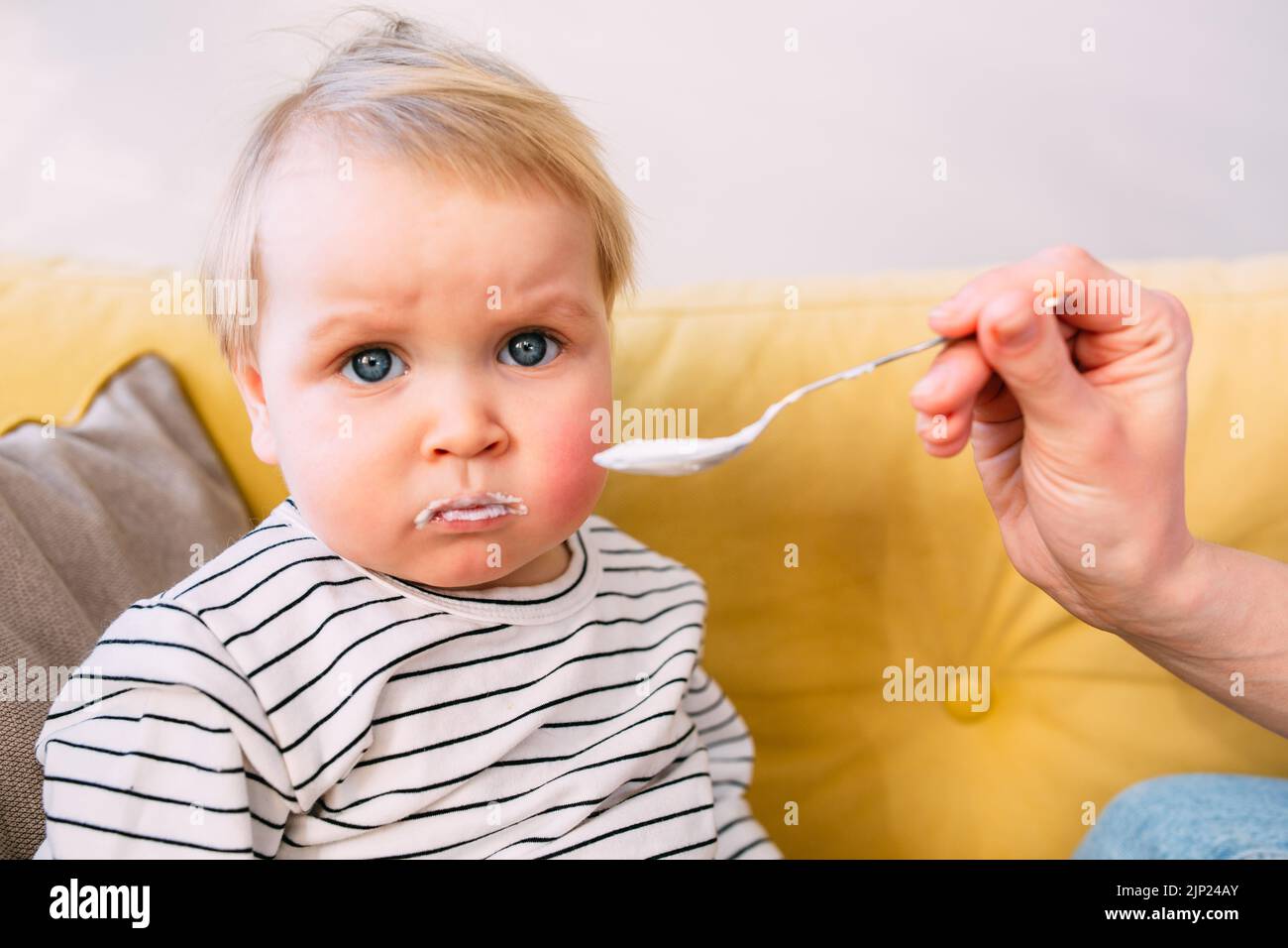 Mom feeds a small child at home with yogurt from a spoon. Family ...