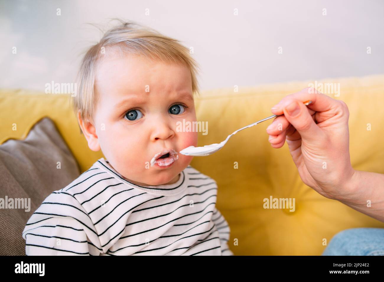 Mom feeds a small child at home with yogurt from a spoon. Family ...