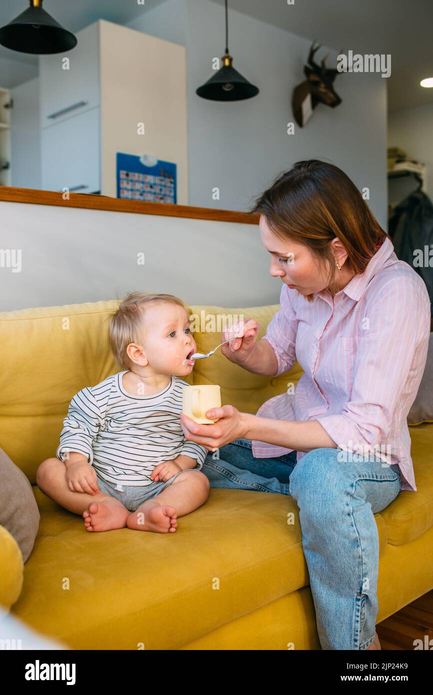 Mom feeds a small child at home with yogurt from a spoon. Family ...