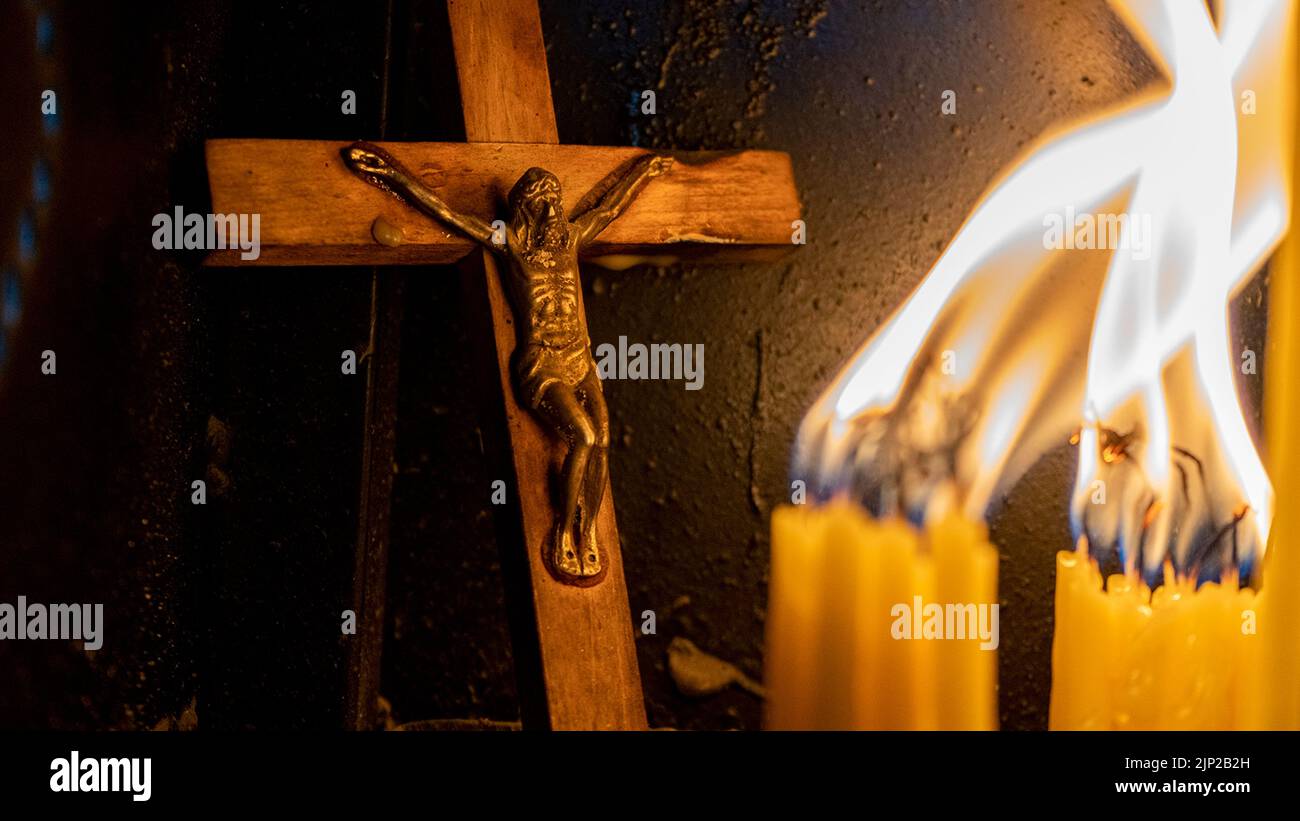 A shallow focus shot of Jesus statue on wooden cross with burning candles in the foreground ...