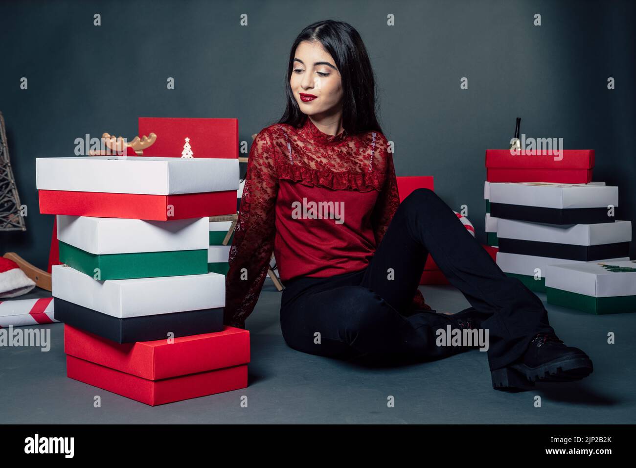 A teen girl sitting on the floor and looking to a tower of Christmas ...
