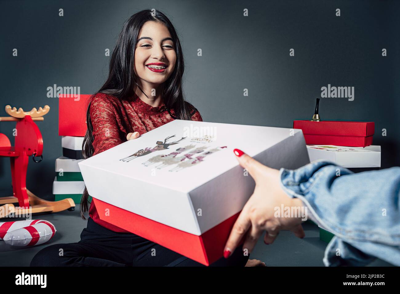 A smiling teen girl sitting on the floor and receiving a Christmas gift ...