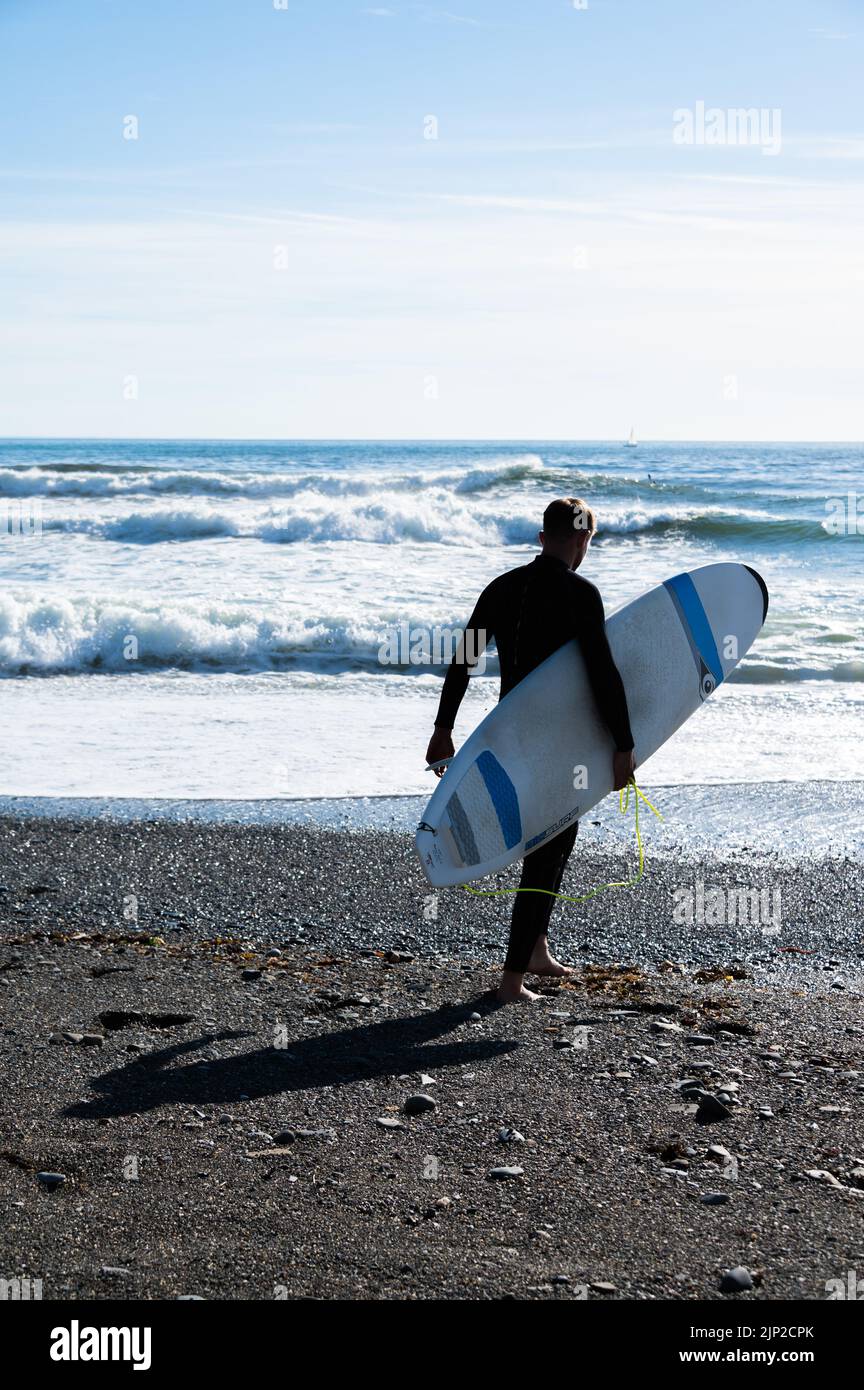 A vertical shot of a surfer holding a surfboard heading into the sea ...