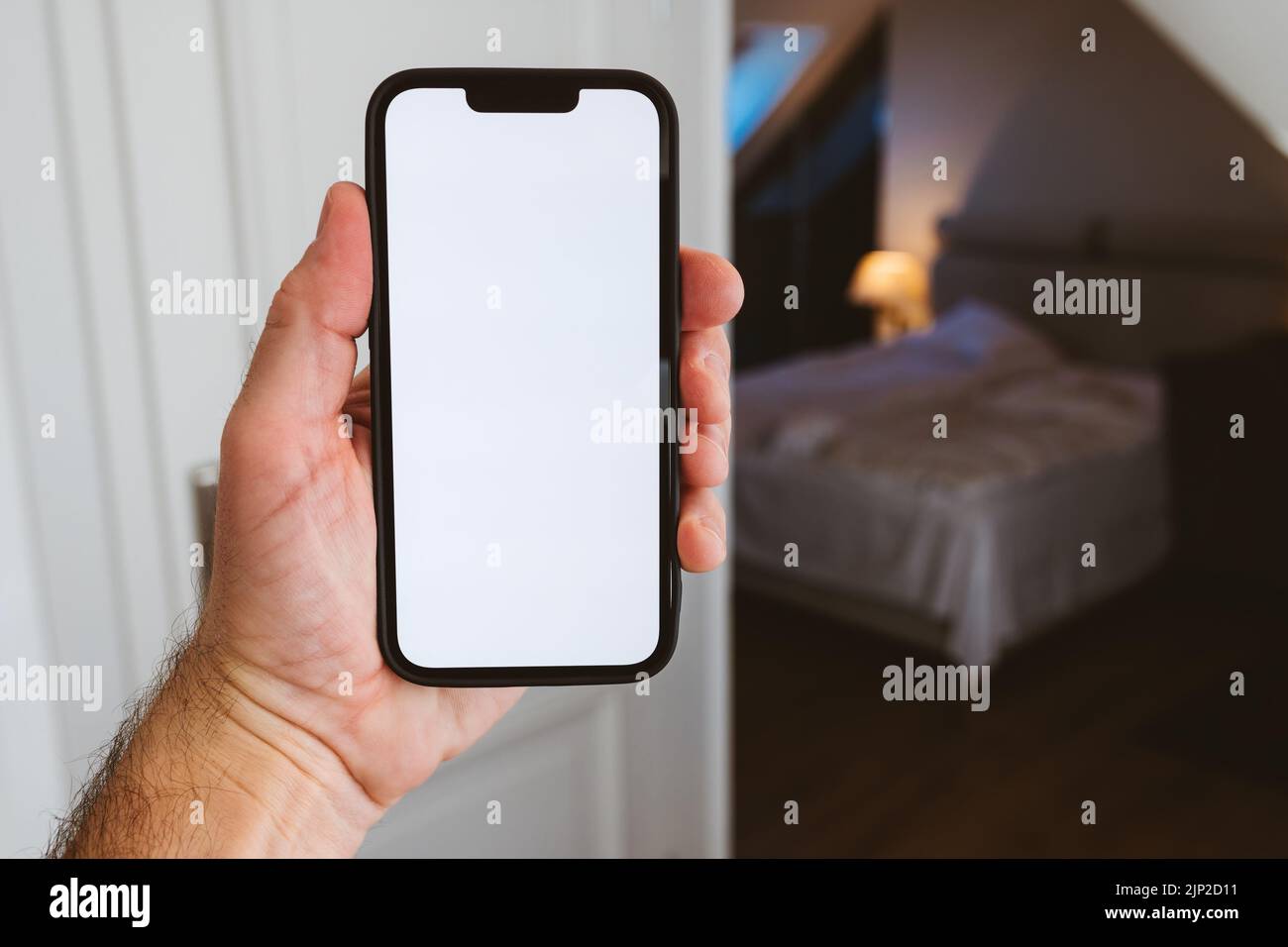 Tourist in hotel bedroom holding smartphone with blank mockup screen ...