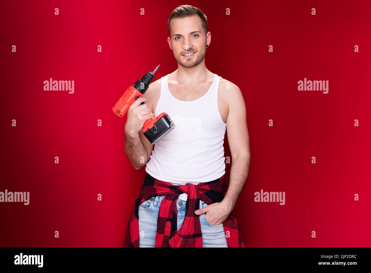 A handsome male in a studio posing with a drill on a red background Stock Photo - Alamy