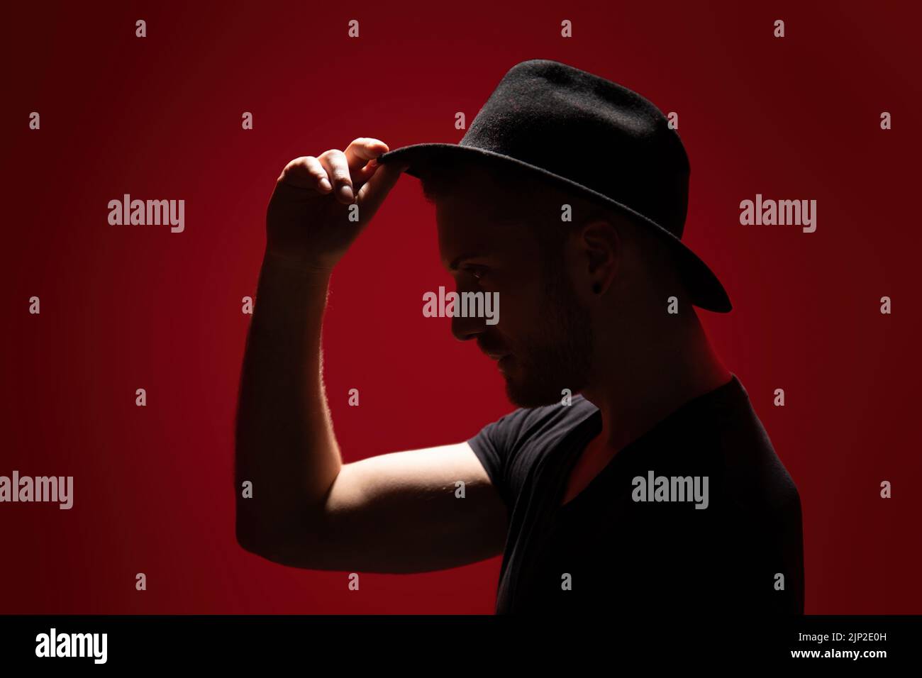 A silhouette of man with hand on hat on front of red background Stock ...