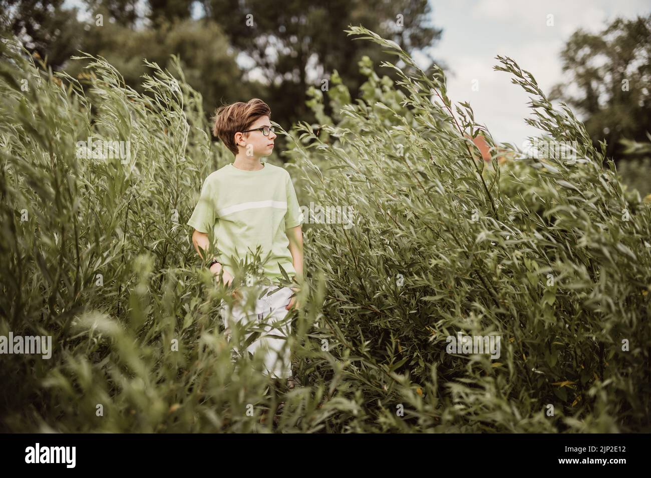 A teen boy walking in a field next to tall green grass Stock Photo - Alamy