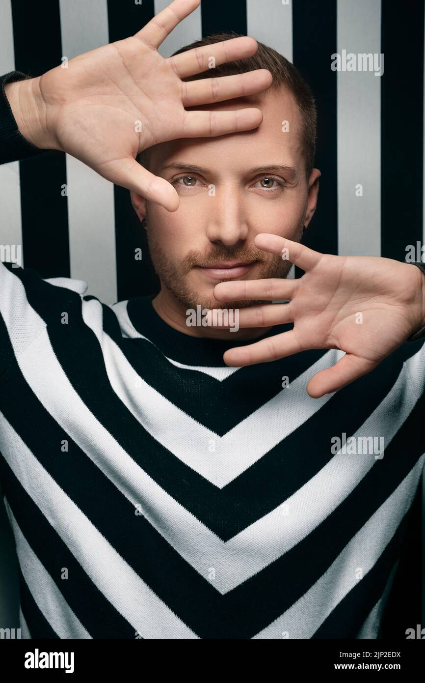 A vertical of a man trying to hide his face with hands wearing a black ...