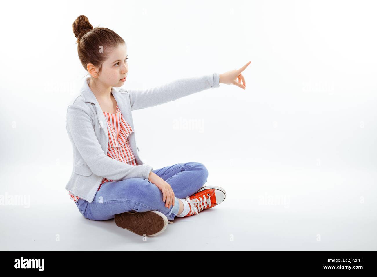 A young girl sitting cross-legged on the floor and pointing at ...