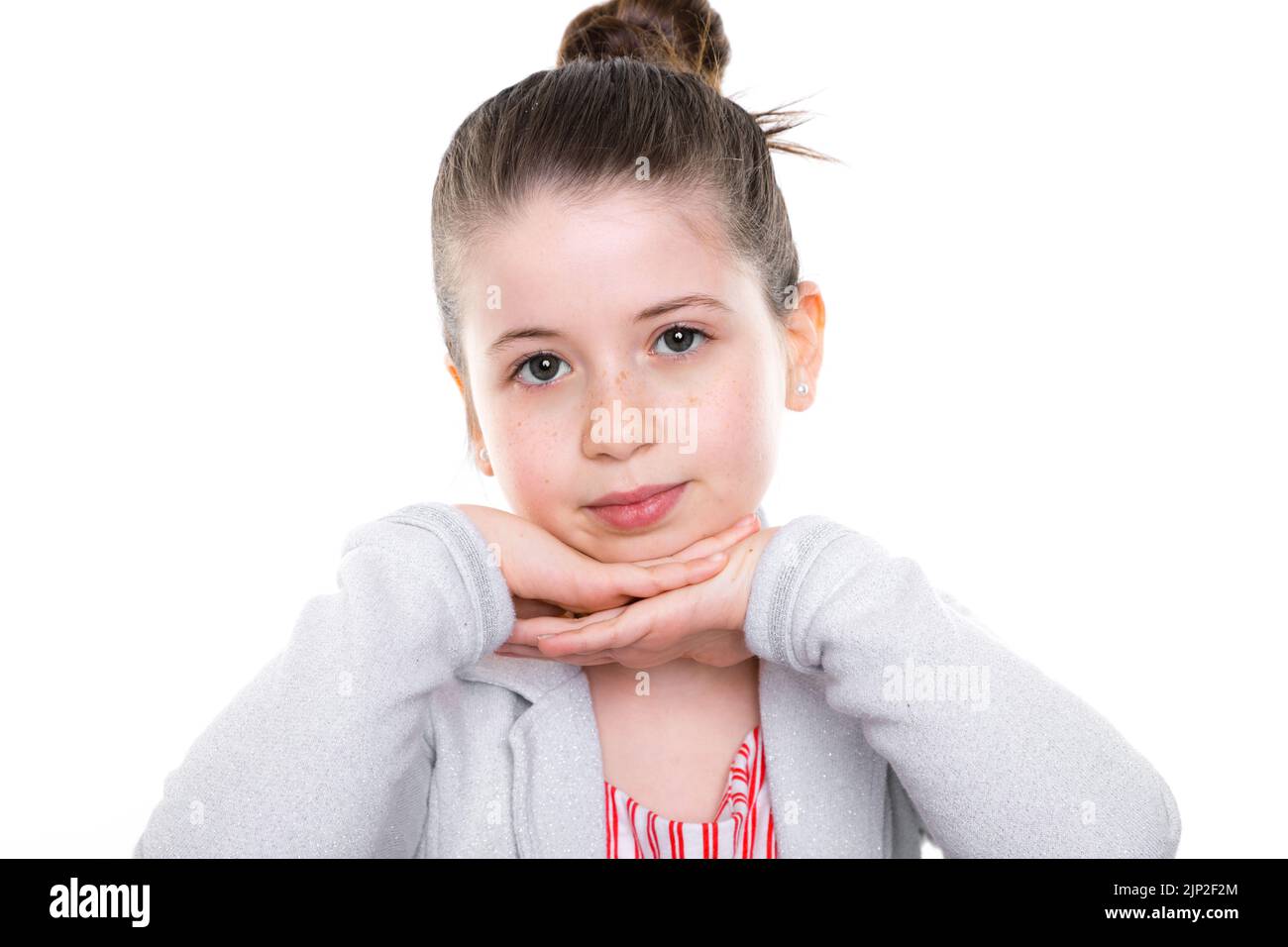 A portrait of a young girl posing with her hands under her chin against ...
